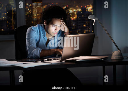 Hispanic man working at the office at night pointing with hand finger ...