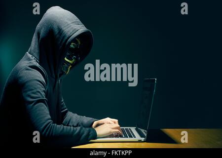 Hooded hacker with mask using laptop to hacking bank system security on ...