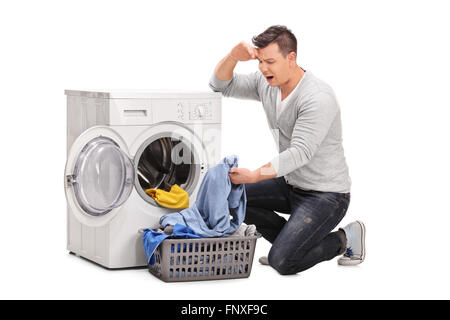 Sad young guy emptying a washing machine isolated on white background ...