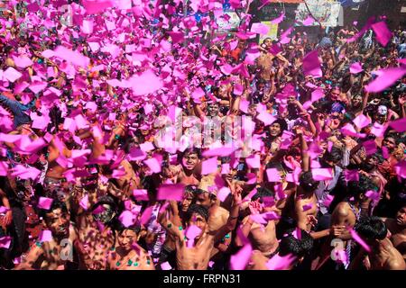 Devotees with color-smeared faces dance on a road during a procession ...