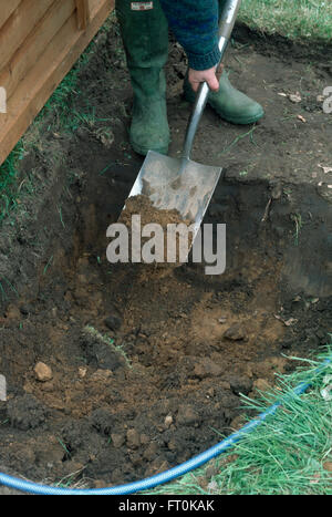 Close-up of a gardener digging out turf before laying hexagonal paving ...