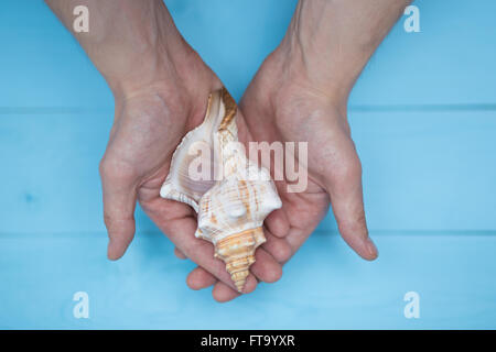 Male fingers hold a seashell on blue wooden background Stock Photo - Alamy