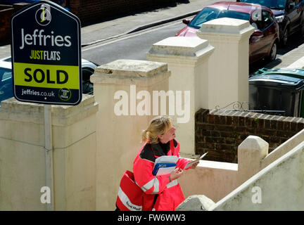 A female Royal Mail postal worker delivering post to a house on her ...