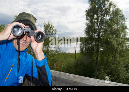 Birdwatcher watching birds with binoculars from behind a bamboo screen ...