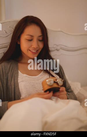 Young asian woman holding alarm clock scared and amazed with open mouth ...