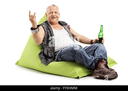 Old punker with a beer bottle seated on a beanbag making a rock hand ...