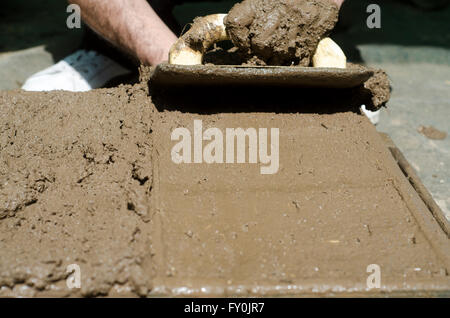 A worker making sustainable mud bricks to construct a greenhouse to ...