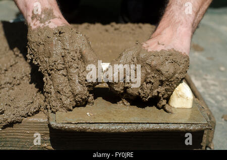 A worker making sustainable mud bricks to construct a greenhouse to ...