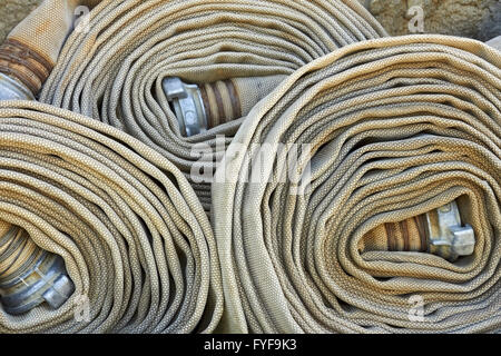 Rolled industrial fire hoses with metal couplings are laying on a rusty ...