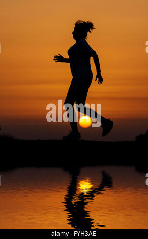 Silhouette woman running against orange sunset with reflection in water ...