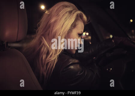 Traffic, aggressive look blonde driving a car at night in the city ...