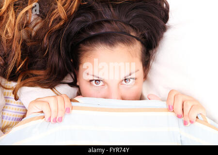 Scared woman hiding under blanket lying on a bed in the night at home ...