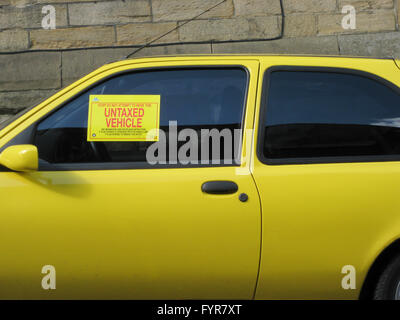 A small yellow car with DVLA Untaxed Vehicle notice in the front window ...