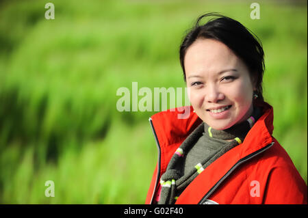 Smiling Chinese woman in green dress smelling perfume while sitting ...
