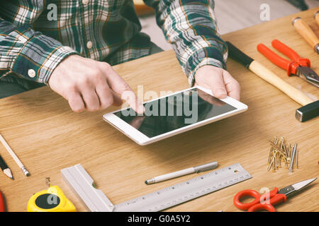 Hands holding construction tools and tablet computer on red background ...