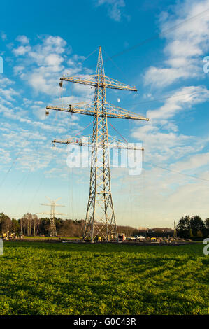 A tall metal power line tower stands among lush green trees. The ...