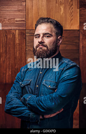 Serious bearded man in casual tshirt holding coffee cup with arm akimbo ...