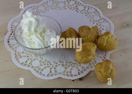Empty Italian bigne next to fresh cream to fill in, on wooden table ...