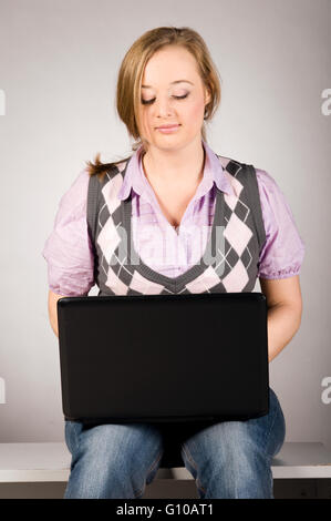 Pretty young female programmer with legs on table showing blank screen ...