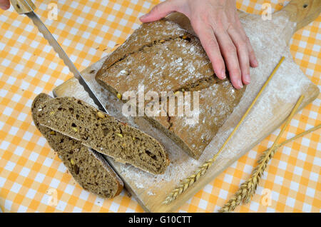 Someone is cutting dark rustic bread with knife Stock Photo - Alamy