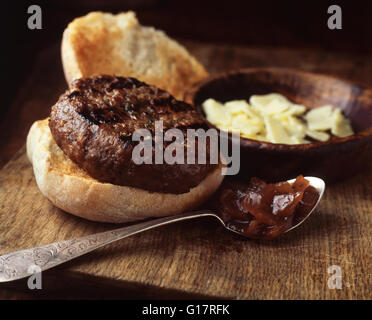 A cheese burger in a crusty bun with lettuce and tomatoes on a chopping ...
