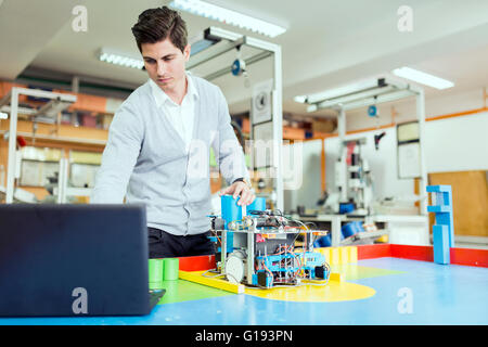 Male electrical engineer programming a robot during robotics class ...
