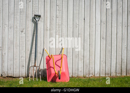 Pitchfork and a wheelbarrow at a fence in a garden Stock Photo - Alamy