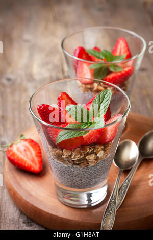 Chia pudding with granola and strawberries in a glass jar on the wooden ...