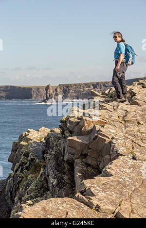 Woman standing on a coastline cliff facing the ocean sunset, raising ...