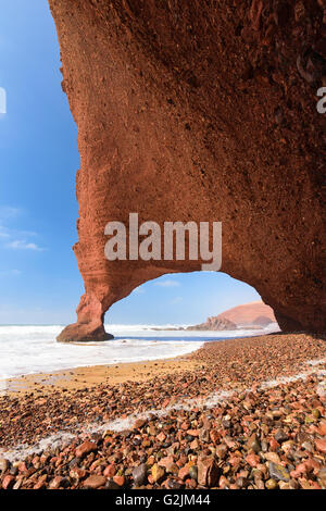 Rocky coastline with red earth, sandy beach and vibrant sky with clouds ...