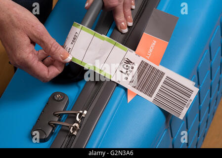 PRIORITY TAG ON A BLUE SUITCASE Airline priority tag being secured to a ...