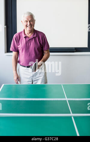 Cheerful senior man playing ping-pong and looking at the camera ...