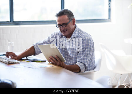 Happy businessman using tablet computer while leaning on desk in office ...
