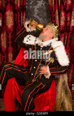 Old funny king getting drunk holding a golden goblet Stock Photo - Alamy