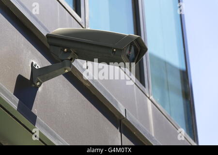 Grey security camera attached to wall blue windows background Stock ...