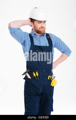 Thoughtful confused builder in helmet scratching his head and holding ...