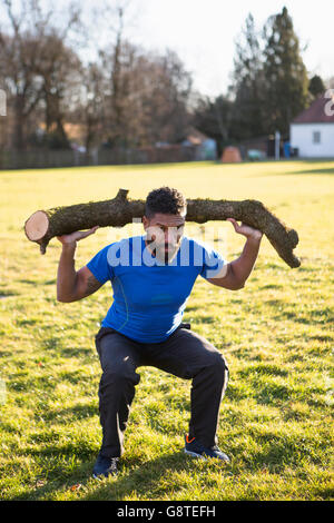Young man doing squats with tree trunk on shoulder Stock Photo - Alamy