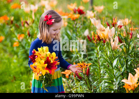 Cute little girl picking lily flowers in blooming summer garden. Child ...