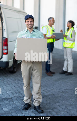 Young hispanic man courier holding package sitting on car at street ...