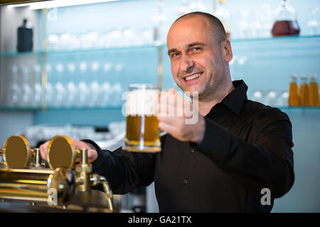 Portrait of bar tender offering beer Stock Photo - Alamy