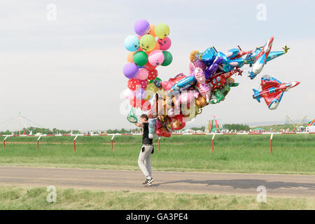 A seller of helium filled balloons shaped as animals stands in the road ...