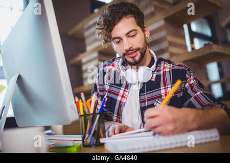 Businessman in headphones writing in notebook while sitting at ...