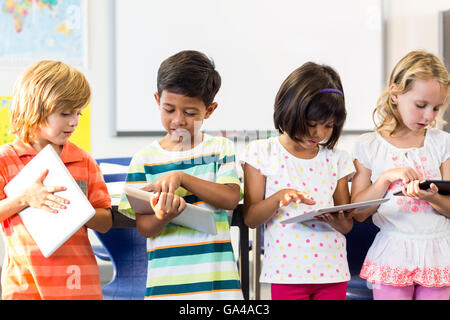 Smiling school kids using tablets in classroom with puzzle hand and ...