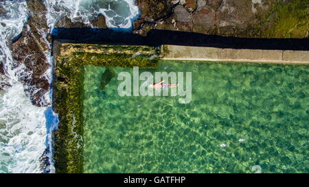 A lone swimmer swims laps in the Austinmer ocean rock pools, viewed ...