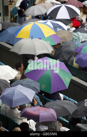 Spectators sit under umbrellas as rain stops play on the outside courts ...
