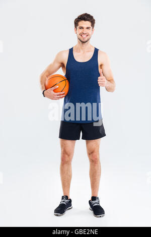 Young sportsman showing his bicep while posing with basketball isolated ...