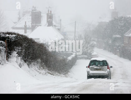 A car makes it’s way through the snowy mountain road near the small ...