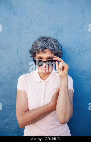 Senior woman with glasses standing over bricks wall sticking tongue out ...