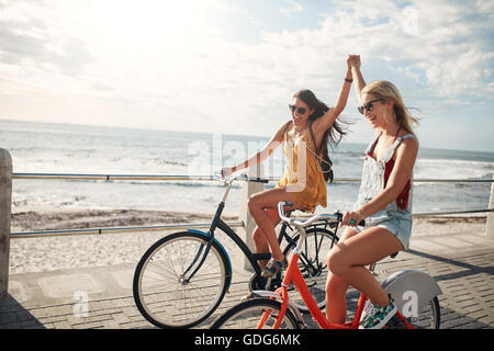 Cheerful friends riding bicycles on road at park. Group of young happy ...
