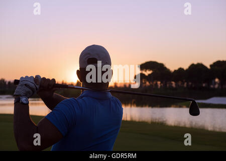 golfer hitting long shot with driver on course at beautiful sunset ...